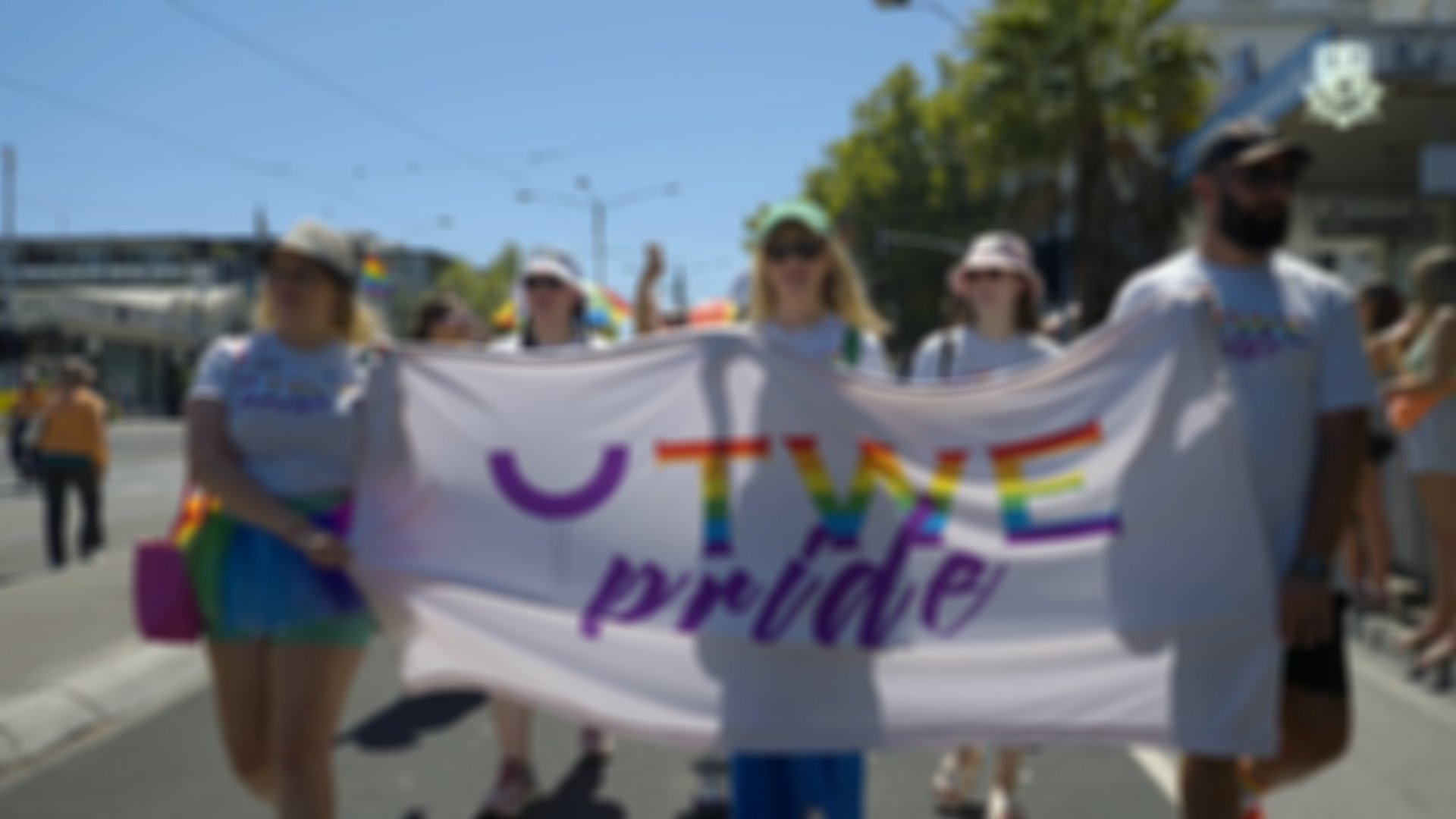 Three people holding up a white banner that reads: TWE Pride
